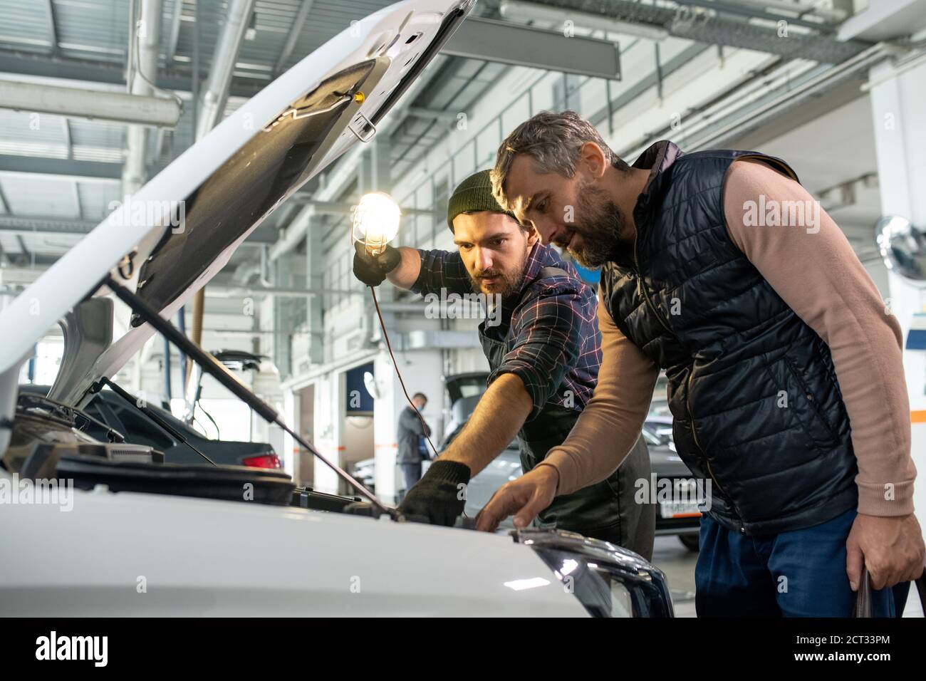 Two young men bending over open car engine compartment during ...
