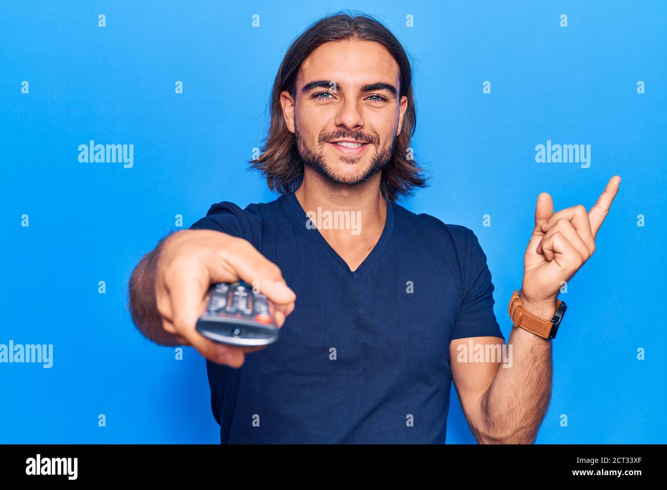 Young handsome man holding television remote control smiling happy ...