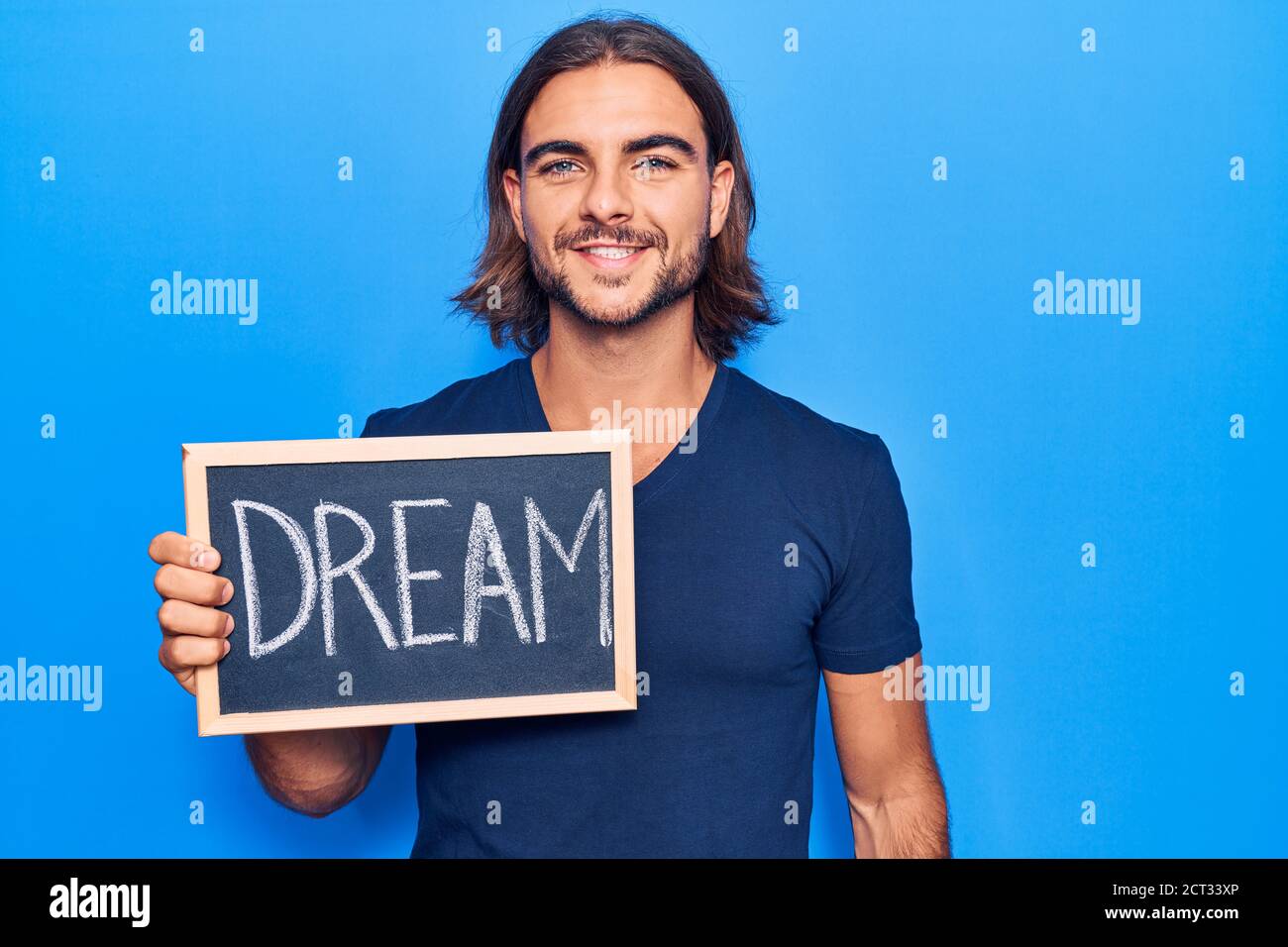 Young handsome man holding blackboard with dream word looking positive ...