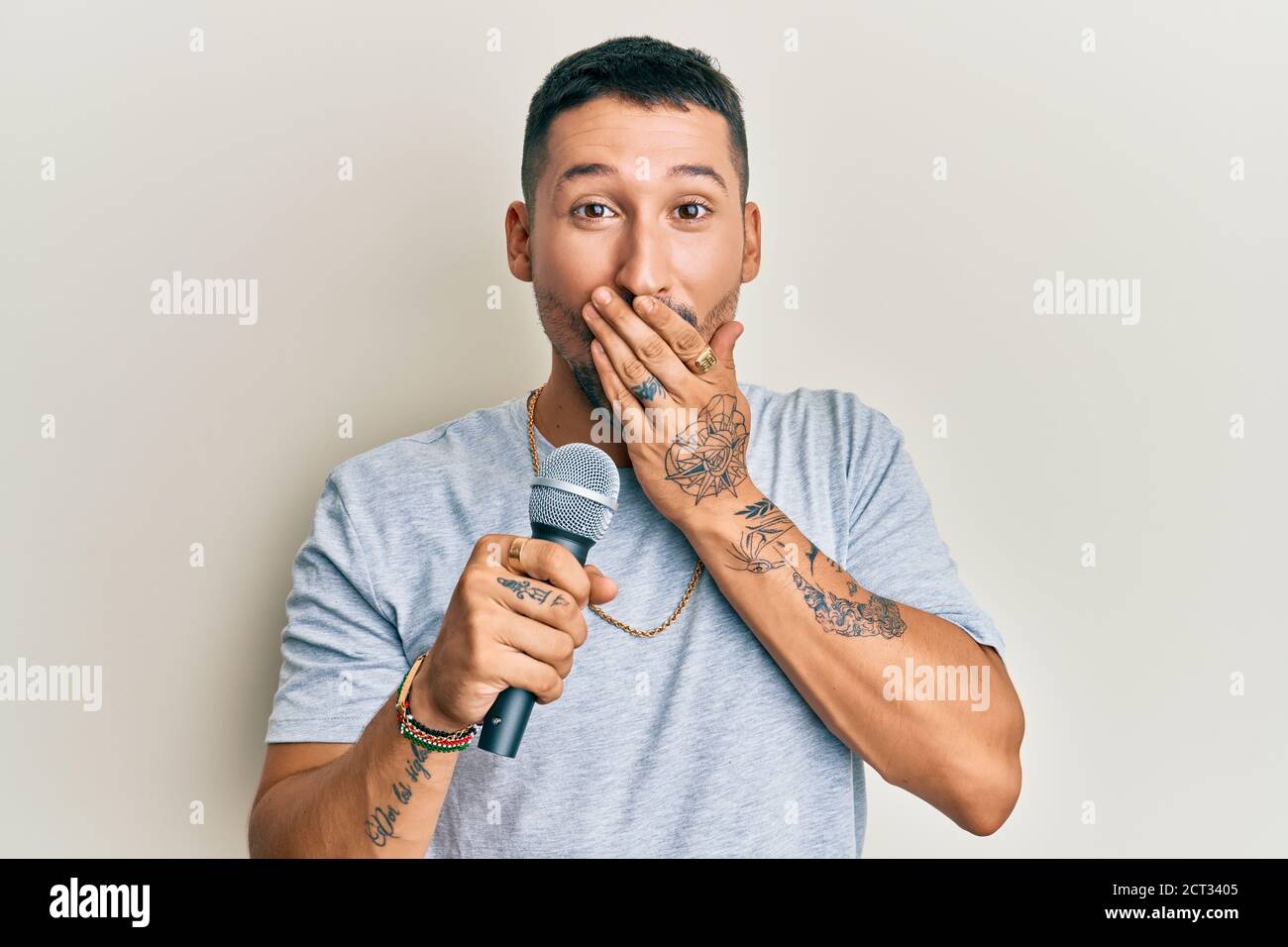Handsome man with tattoos singing song using microphone covering mouth ...