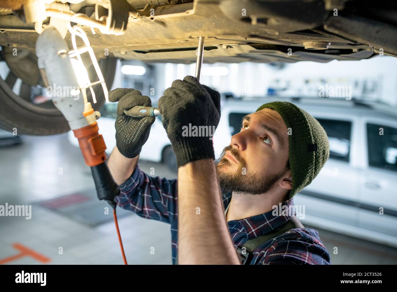 Young bearded repairman in gloves and uniform using handtool to fix ...
