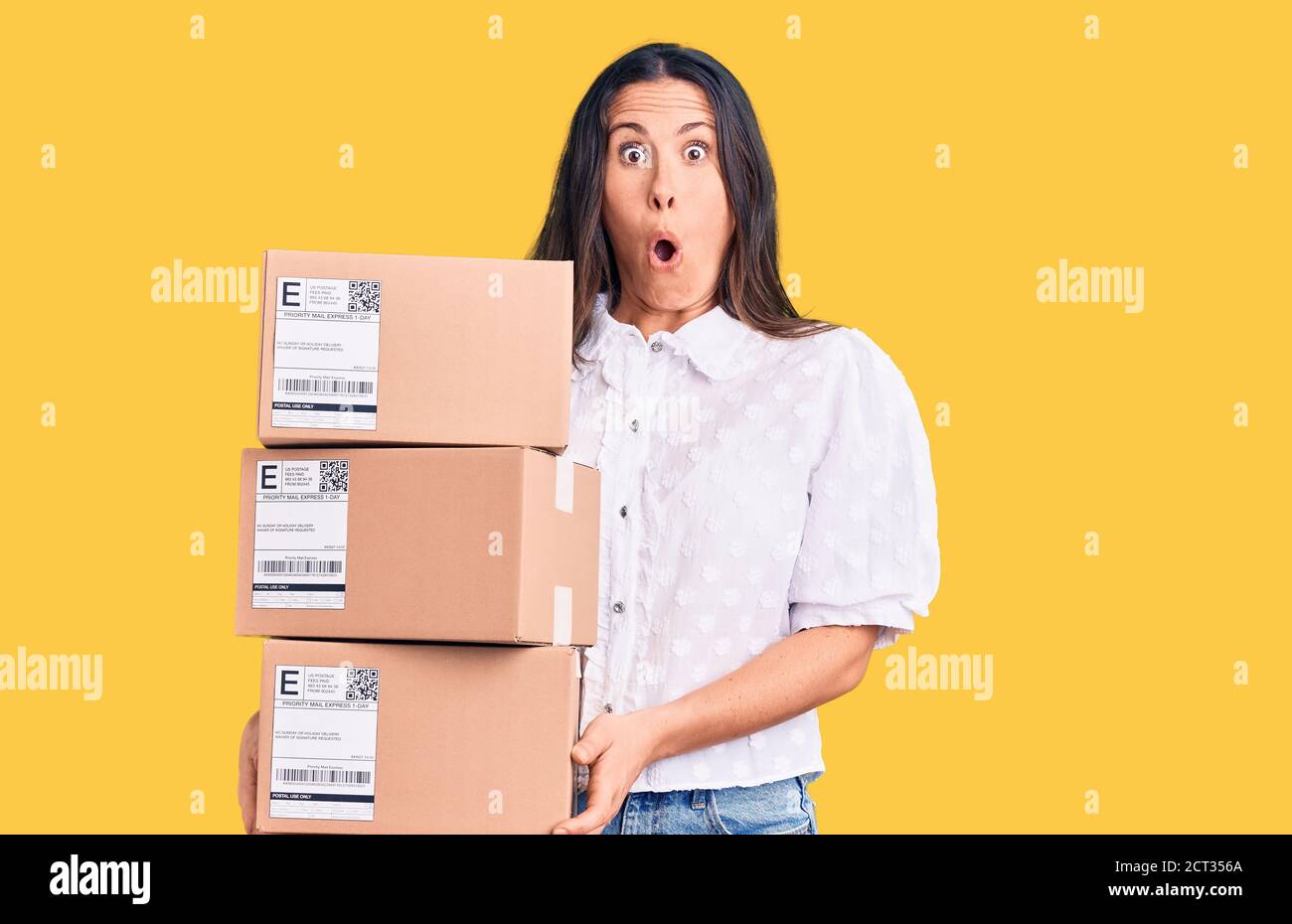 Young beautiful brunette woman holding delivery cardboard package ...