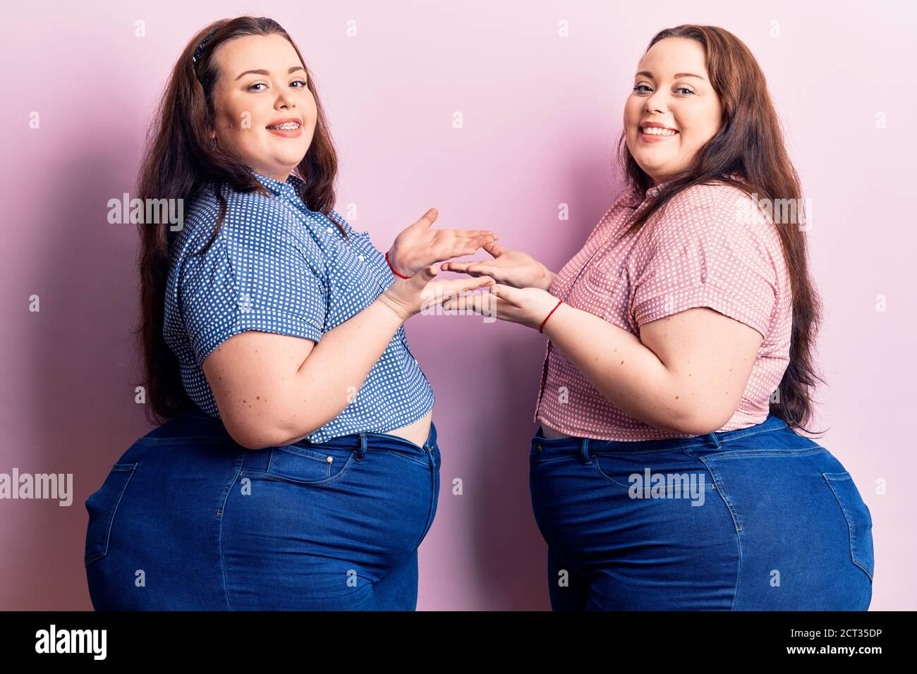 Young plus size twins wearing casual clothes pointing aside with hands ...