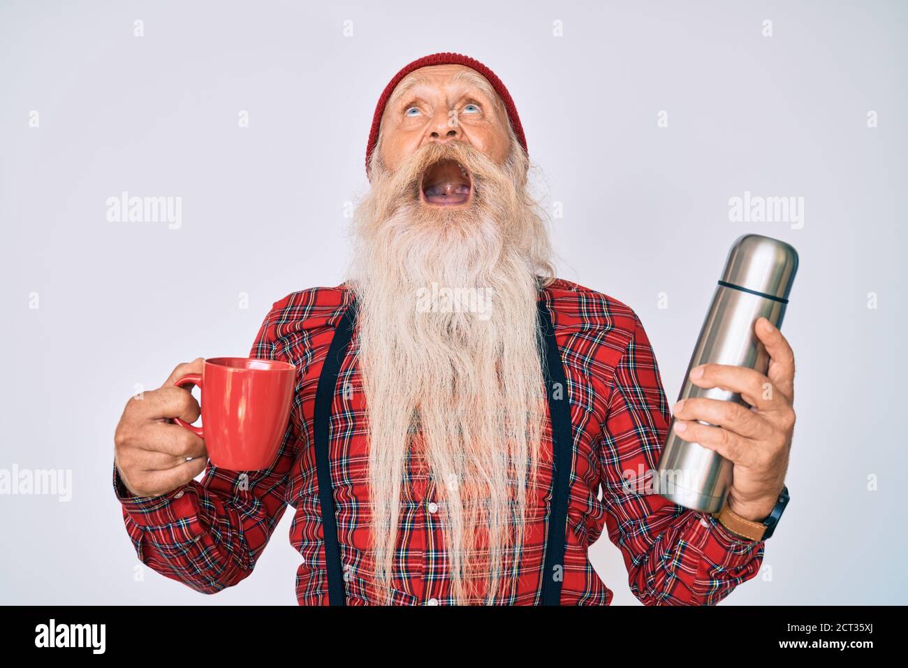 Old senior man with grey hair and long beard holding cup of coffee and ...
