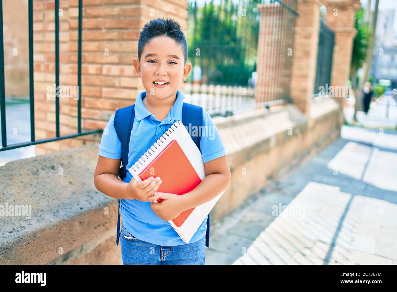 Adorable student boy smiling happy holding book at street of city Stock ...