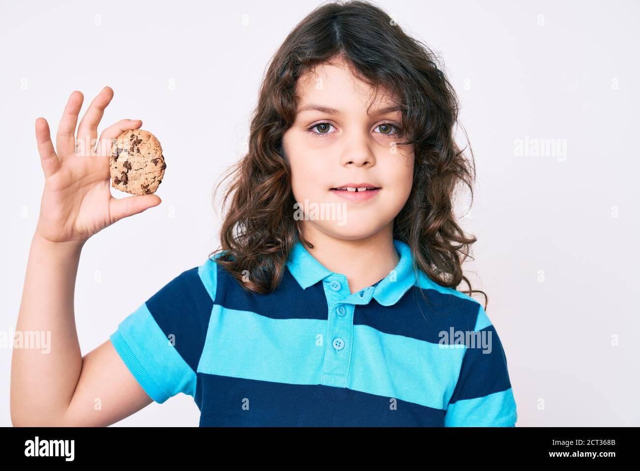 Cute hispanic child with long hair holding cookie looking positive and ...