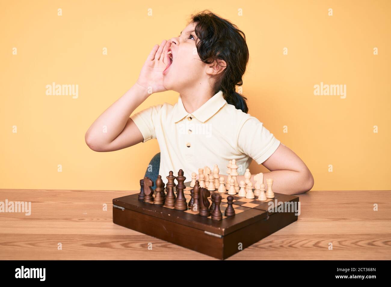 Cute hispanic child playing chess sitting on the table shouting and ...