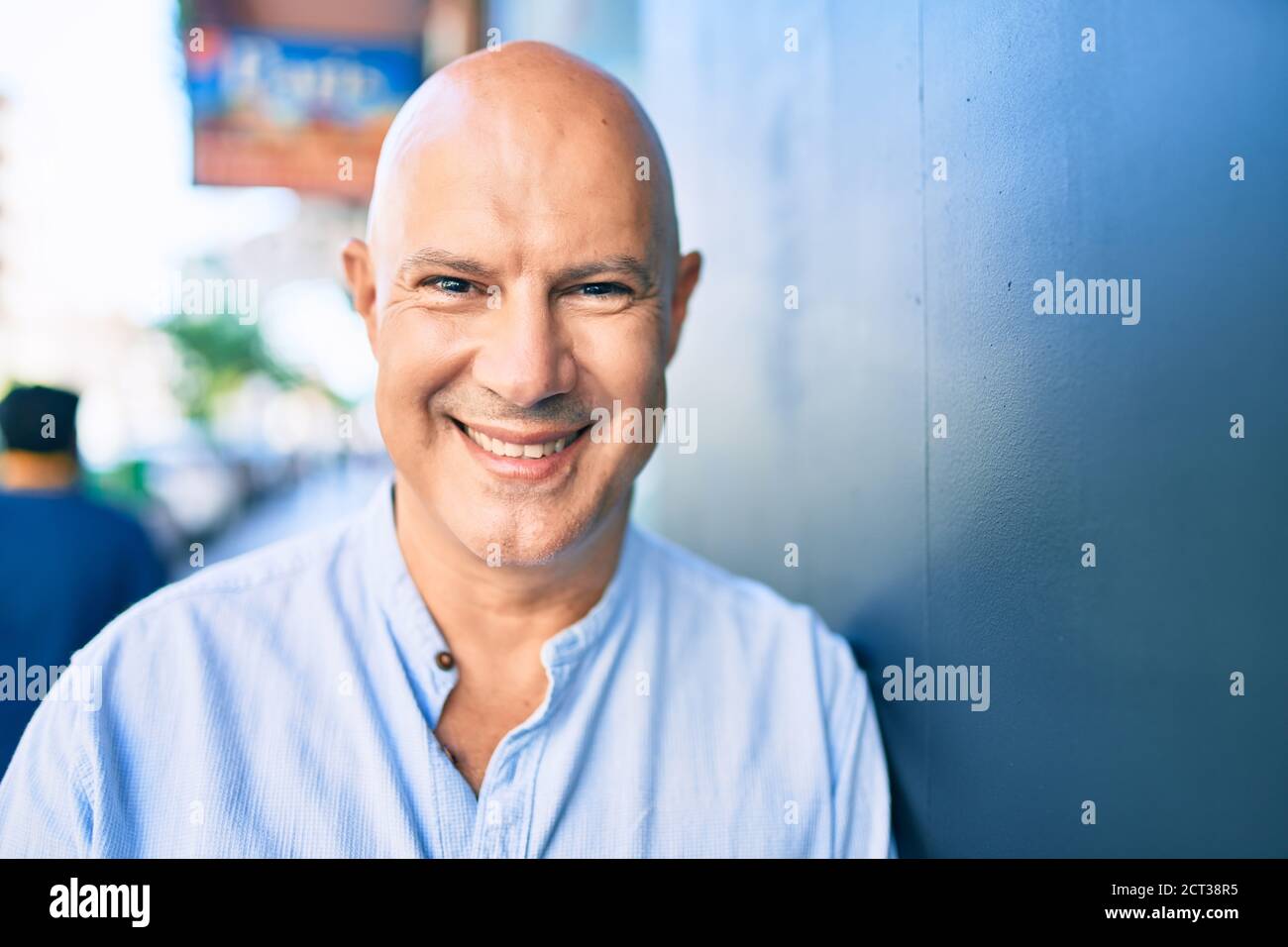 Middle age bald man smiling happy leaning on the wall at the city Stock ...