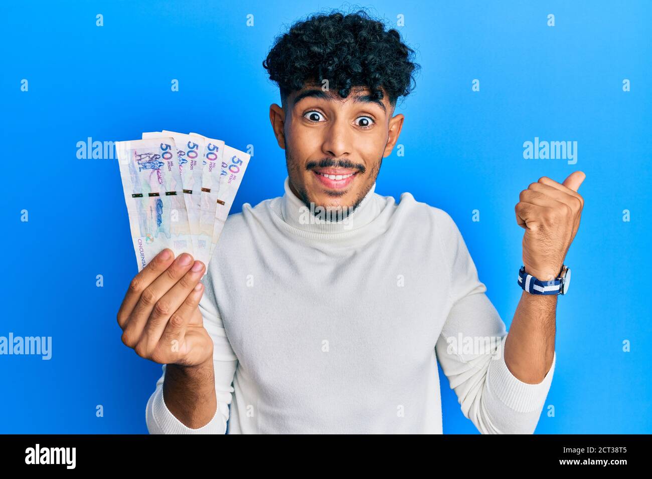 Young arab handsome man holding 50 colombian pesos banknotes screaming ...