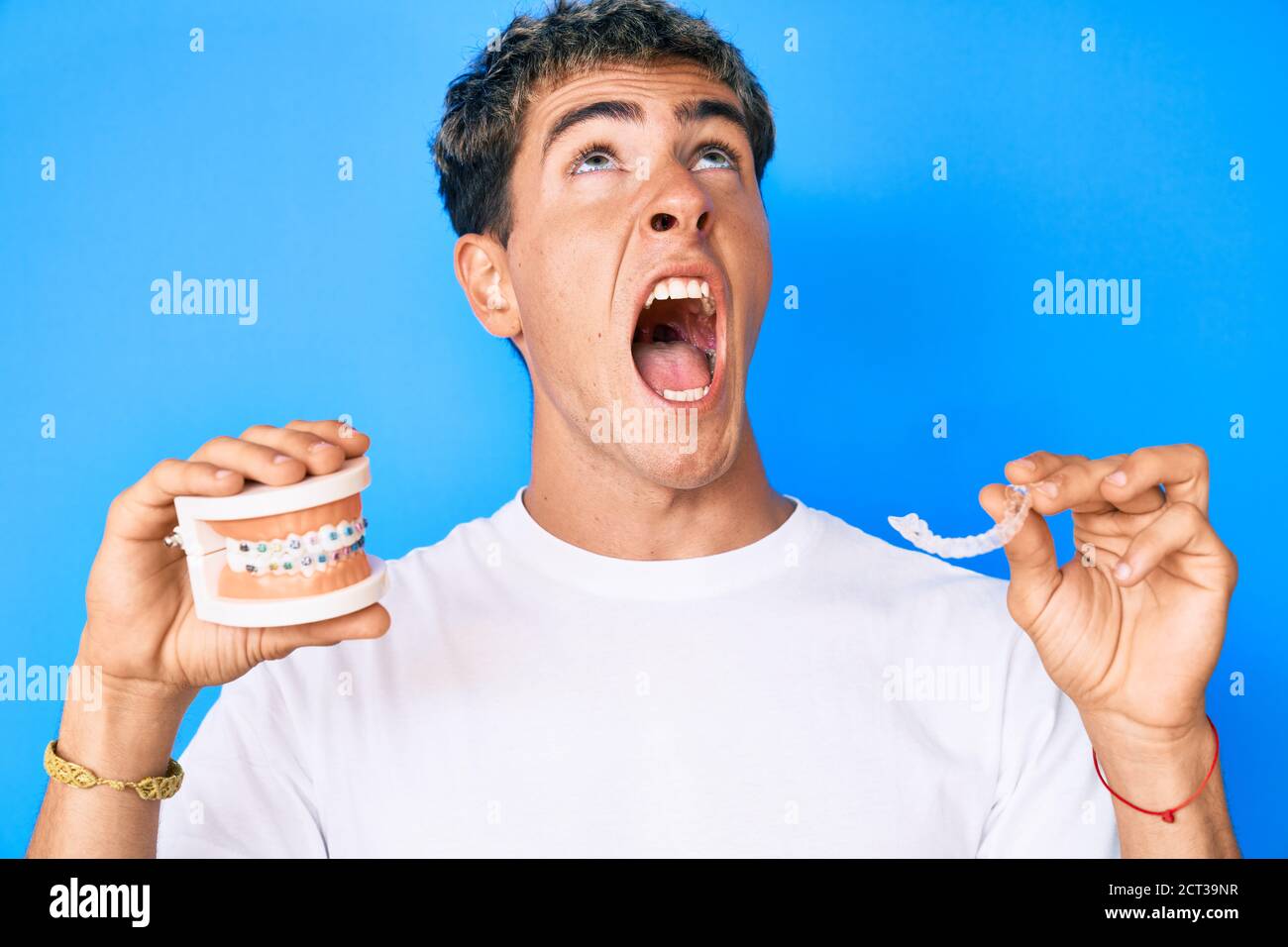 Young handsome man holding orthodontic angry and mad screaming ...