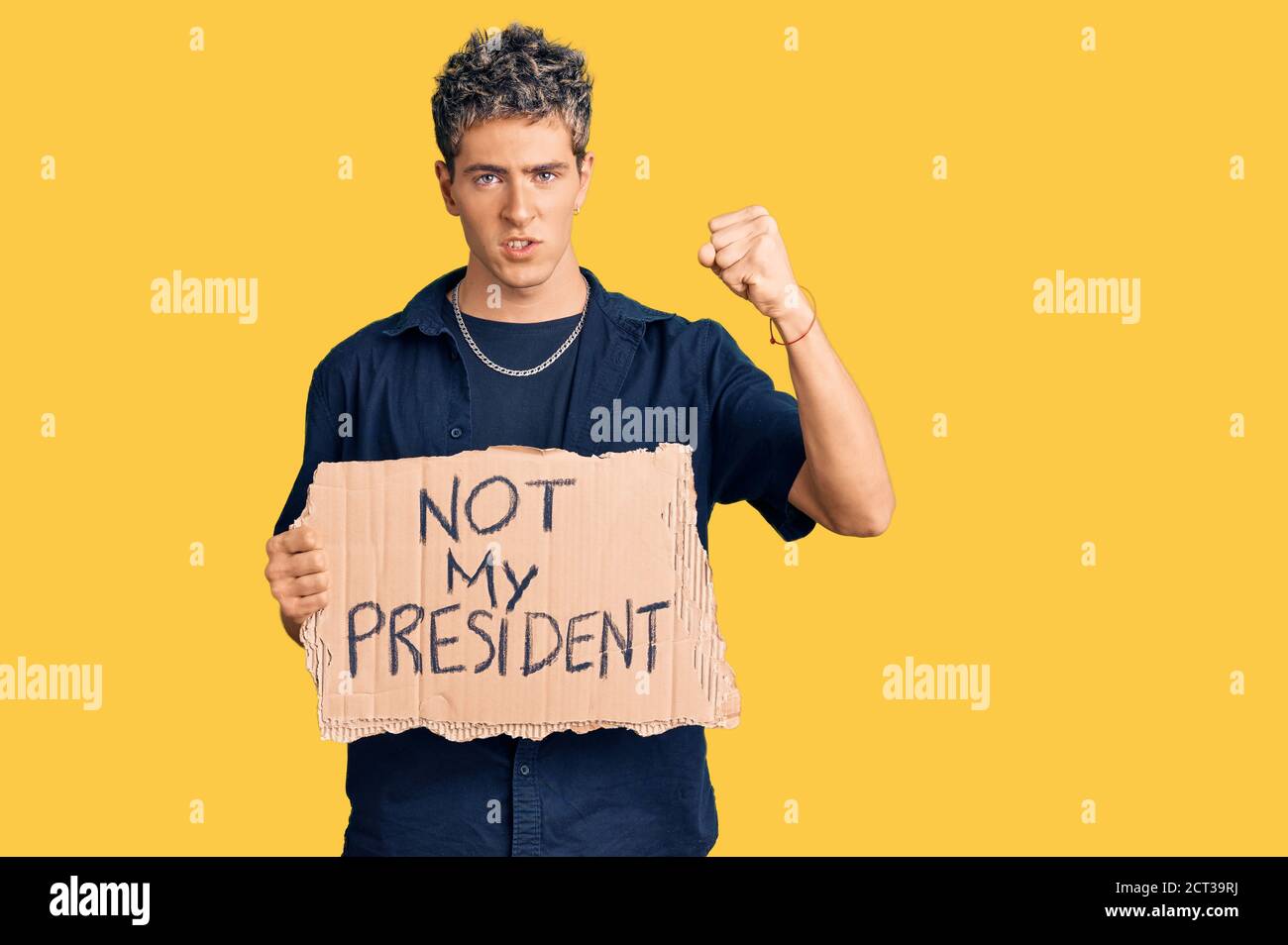 Young handsome man holding not my president protest banner annoyed and ...