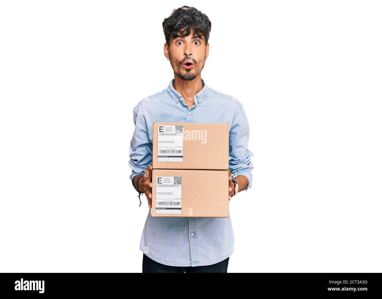 Young hispanic man holding delivery package scared and amazed with open ...
