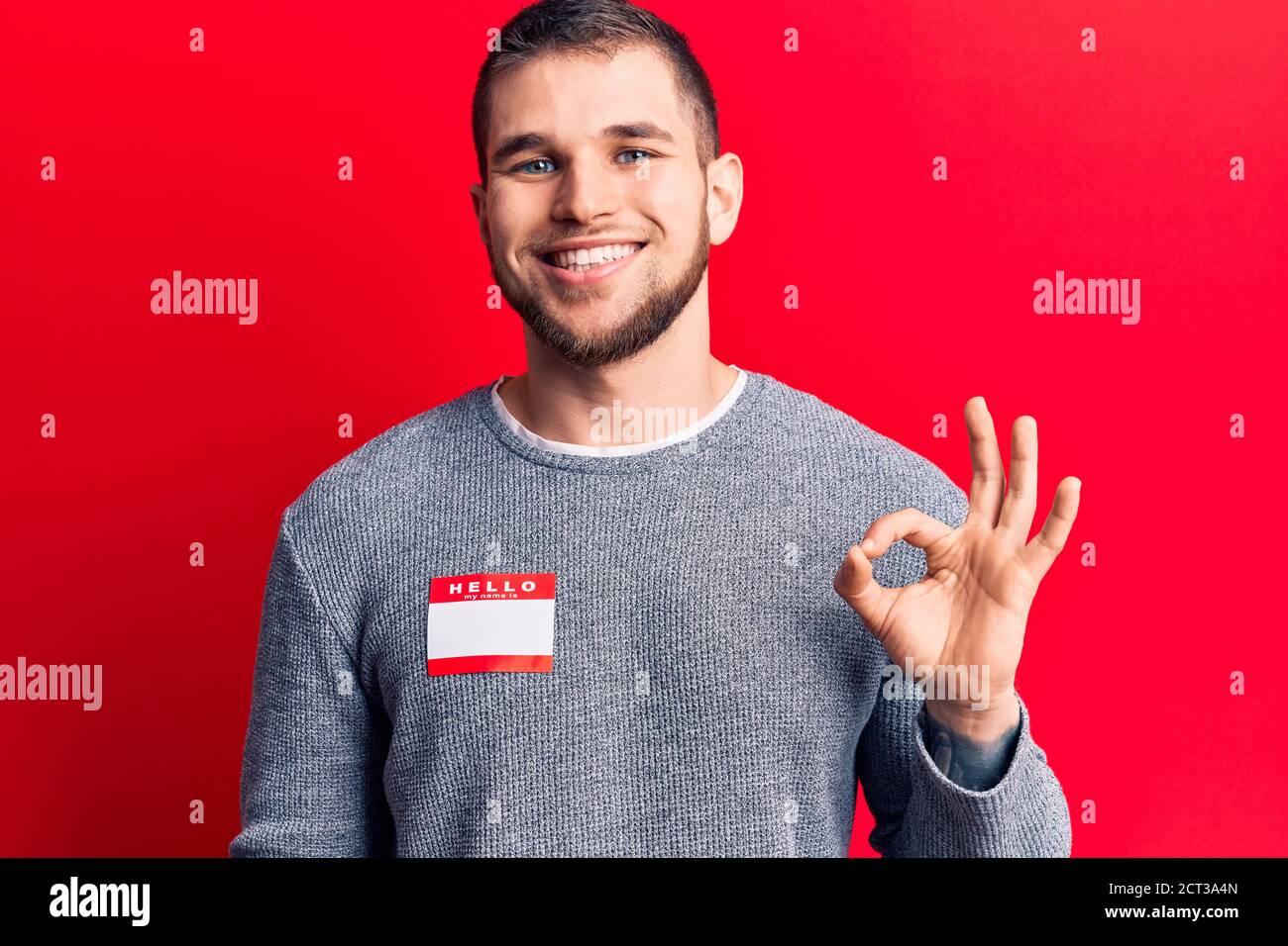 Young handsome man wearing hello my name is sticker doing ok sign with ...