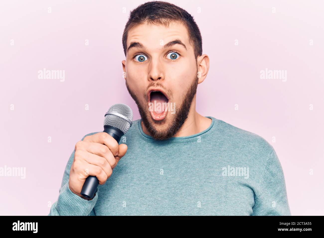 Young handsome man singing song using microphone scared and amazed with ...