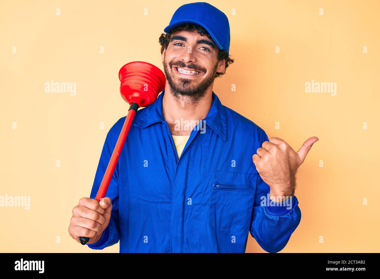 Handsome young man with curly hair and bear wearing plumber uniform ...