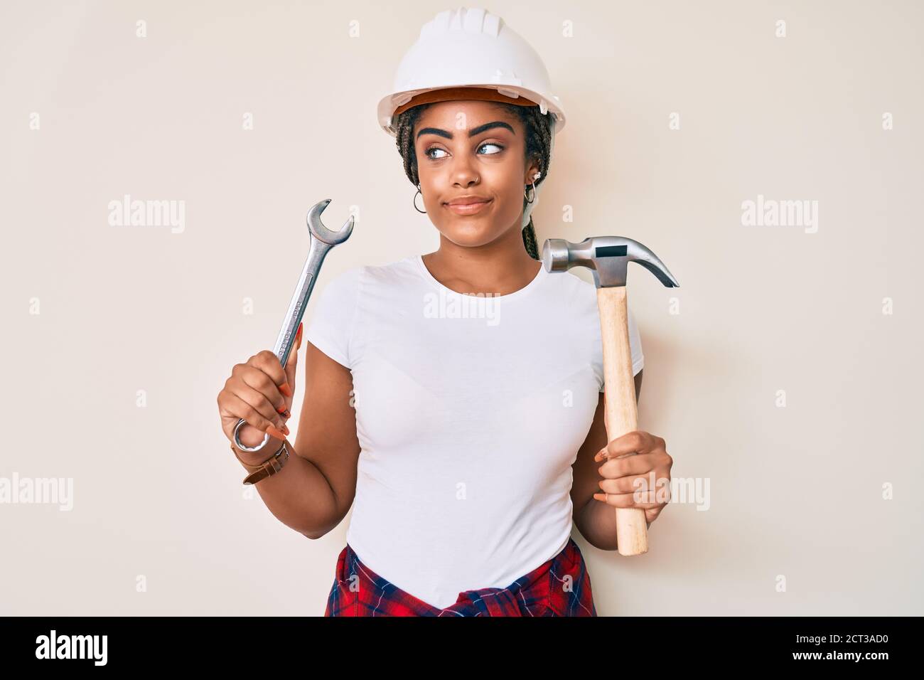 Young african american woman with braids wearing hardhat holding hammer ...