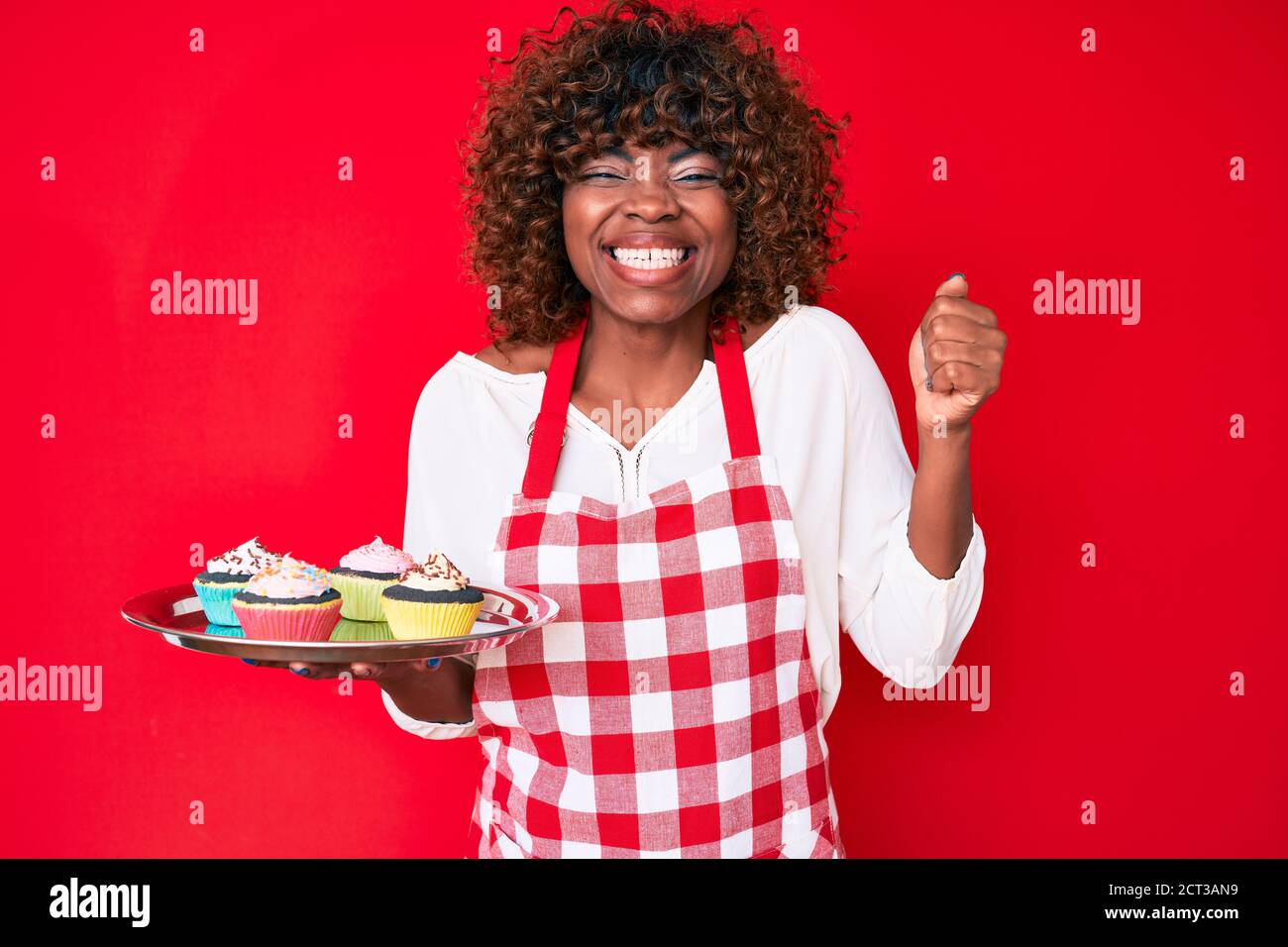 Young african american woman wearing apron holding cupcake screaming ...