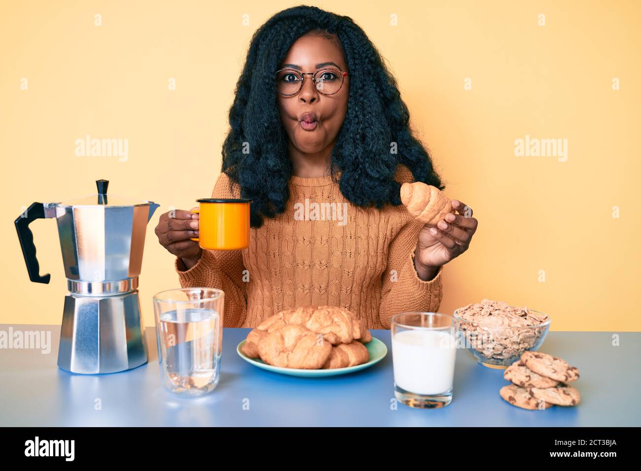 Young african american woman eating breakfast holding croissant making ...