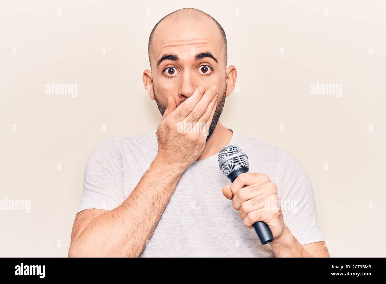 Young handsome bald man singing song using microphone covering mouth ...