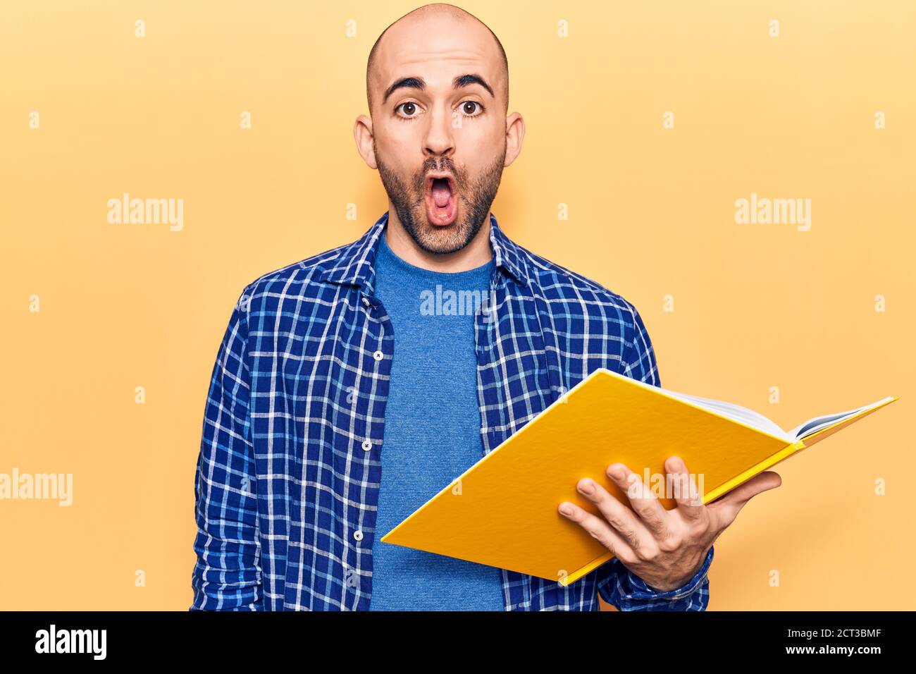 Young handsome bald man reading book scared and amazed with open mouth ...