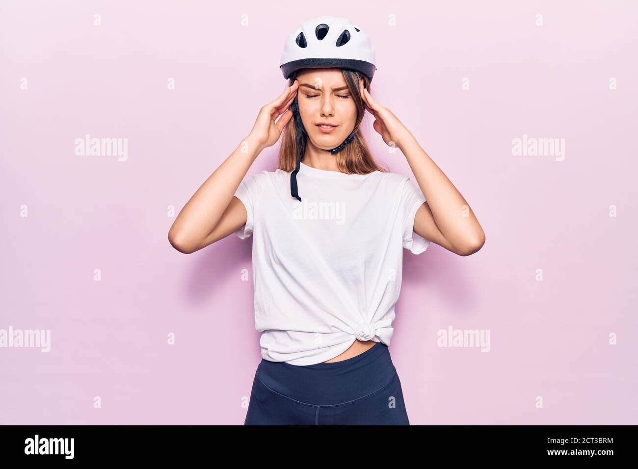 Young beautiful girl wearing bike helmet with hand on head, headache ...