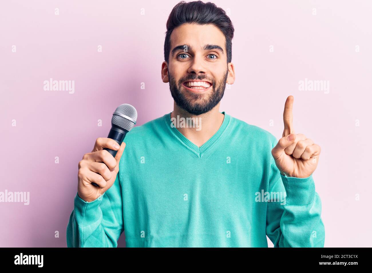Young handsome man with beard singing song using microphone smiling ...