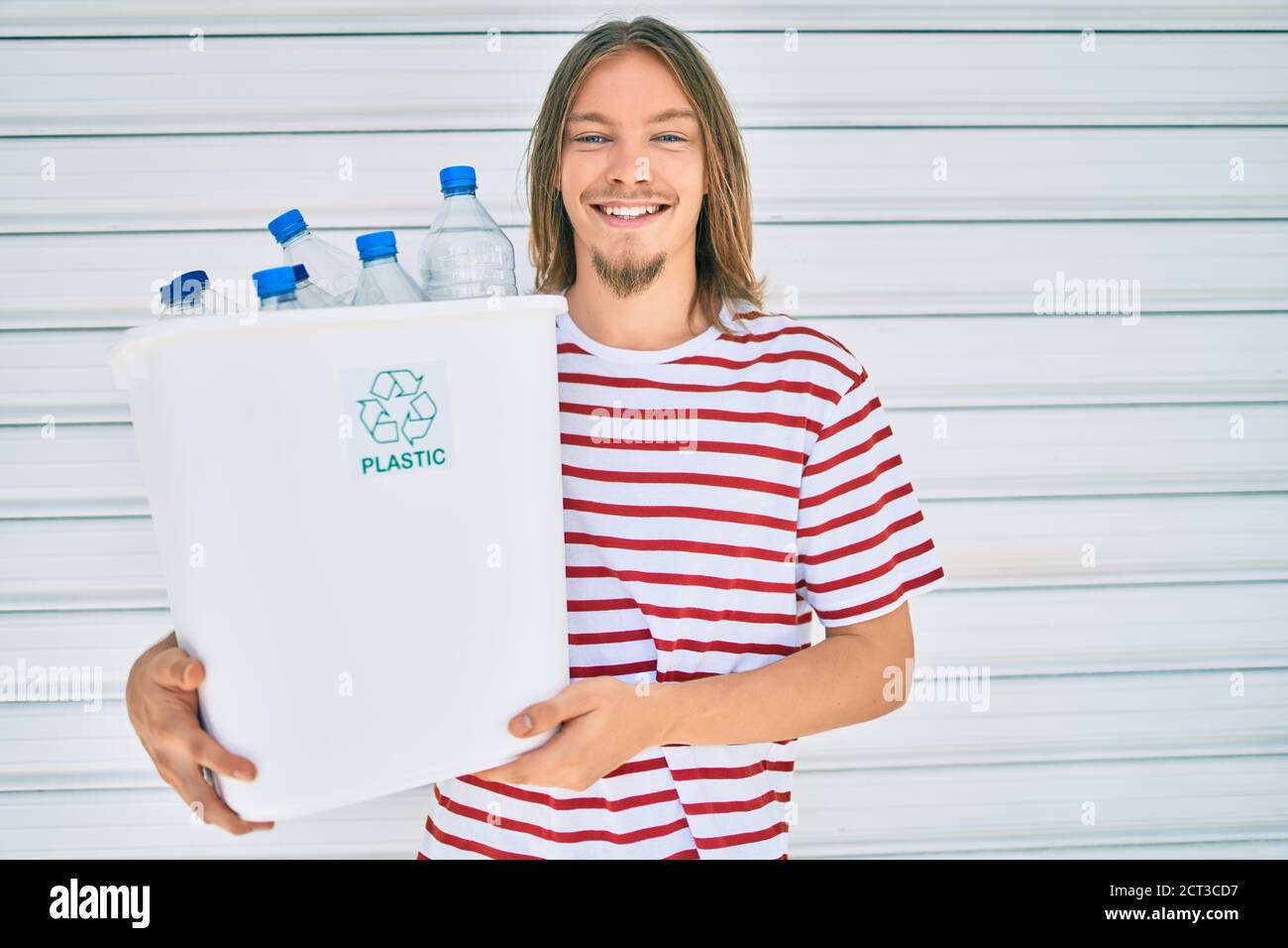 Young caucasian man with blond long hair and beard recycling plastic ...