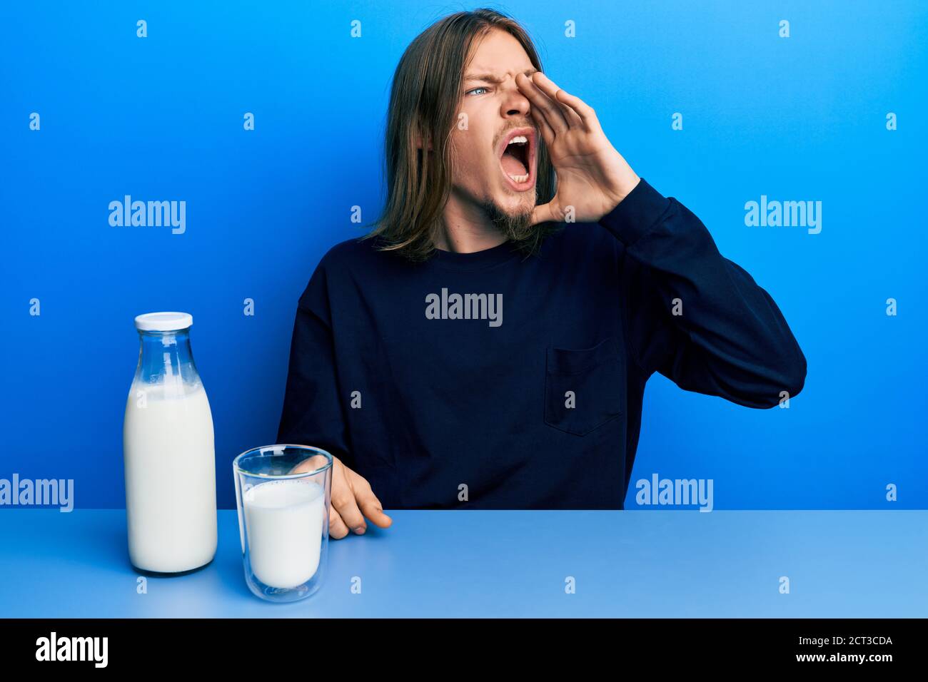 Handsome caucasian man with long hair holding glass of milk shouting ...