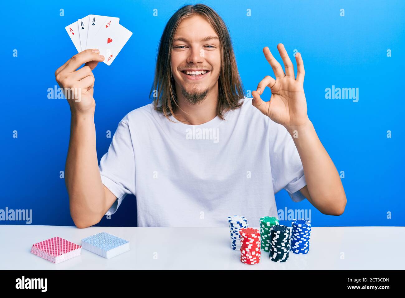 Handsome caucasian man with long hair playing poker holding cards doing ...