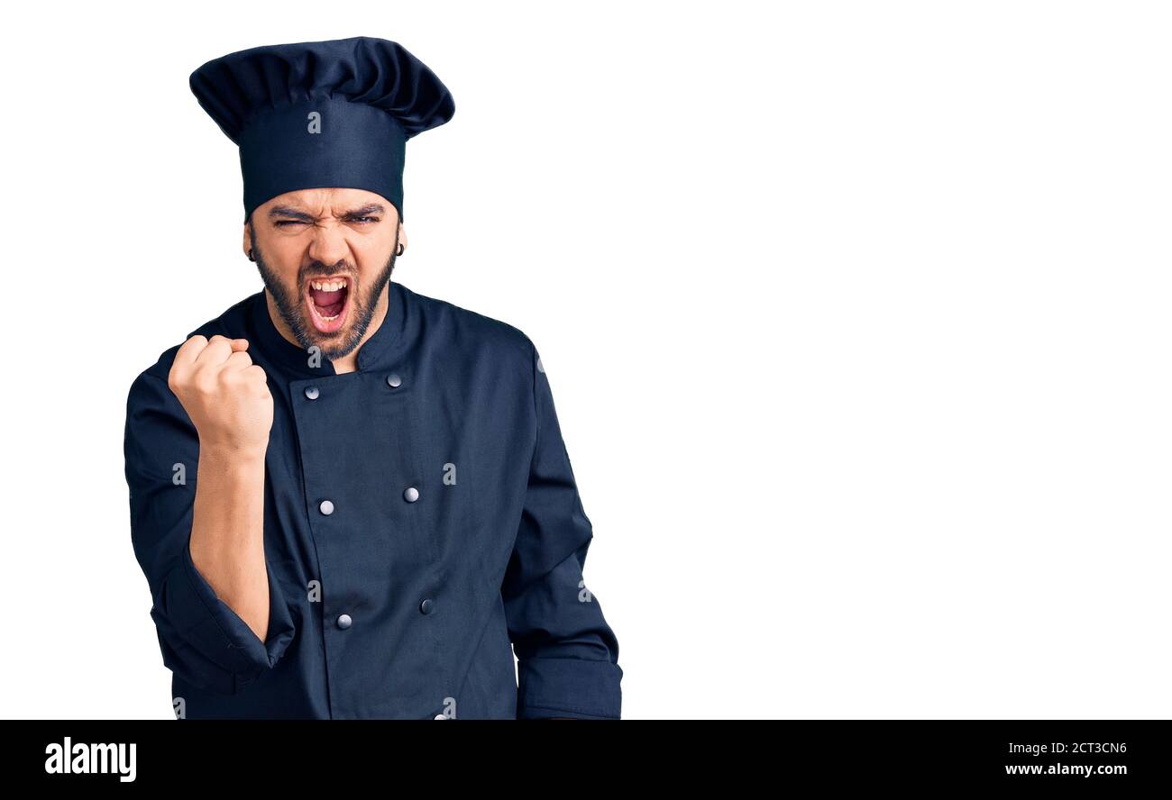 Young hispanic man wearing cooker uniform angry and mad raising fist ...