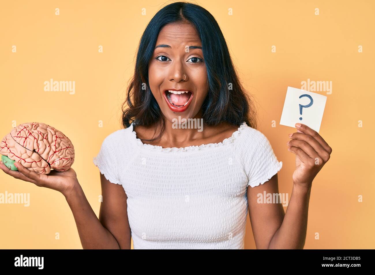 Young indian girl holding brain and question mark reminder smiling and ...