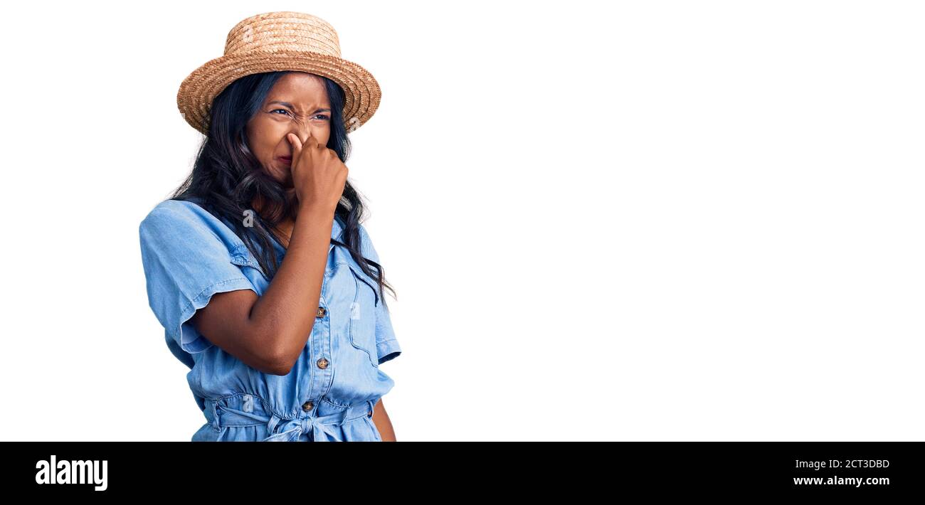 Young indian girl wearing summer hat smelling something stinky and ...