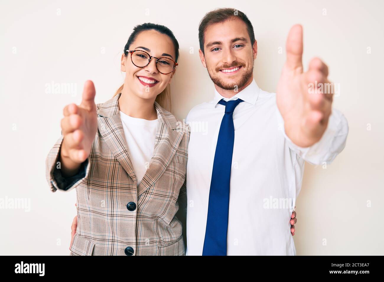 Beautiful couple wearing business clothes smiling friendly offering ...