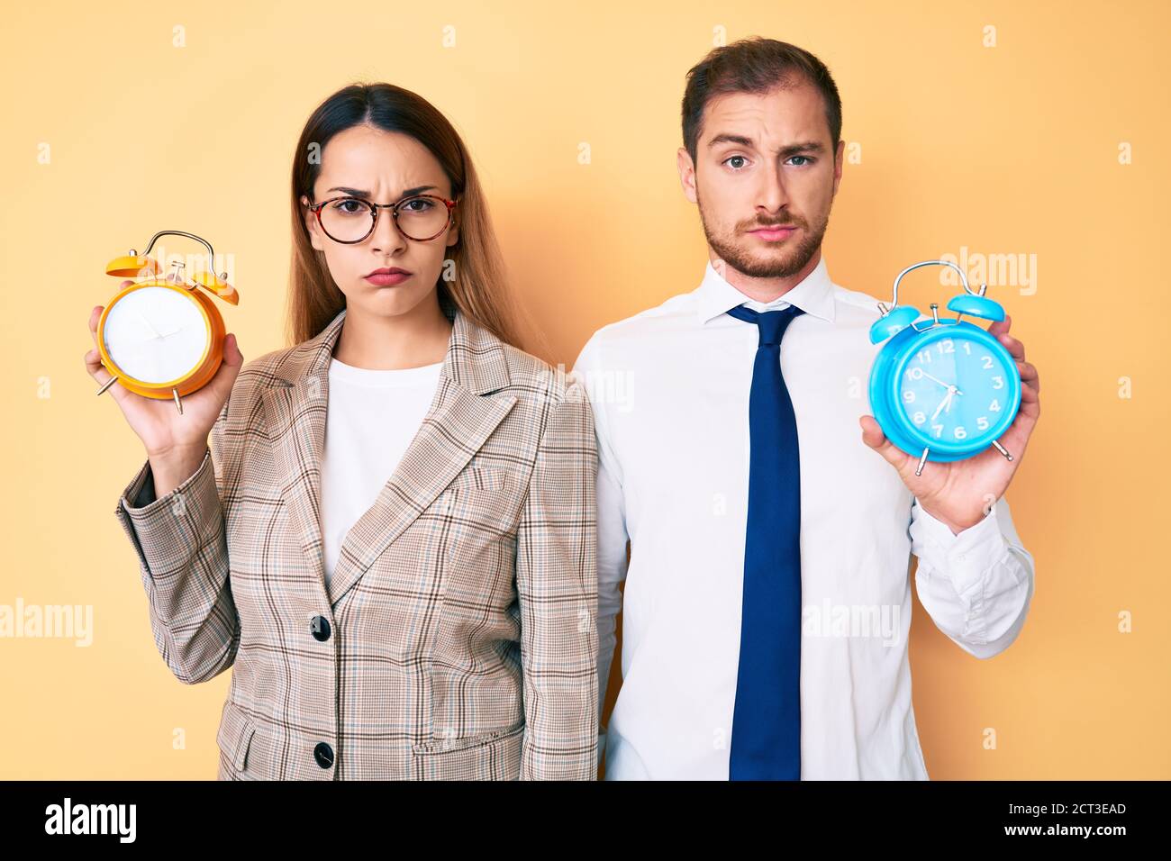 Beautiful couple wearing business jacket and holding alarm clock ...