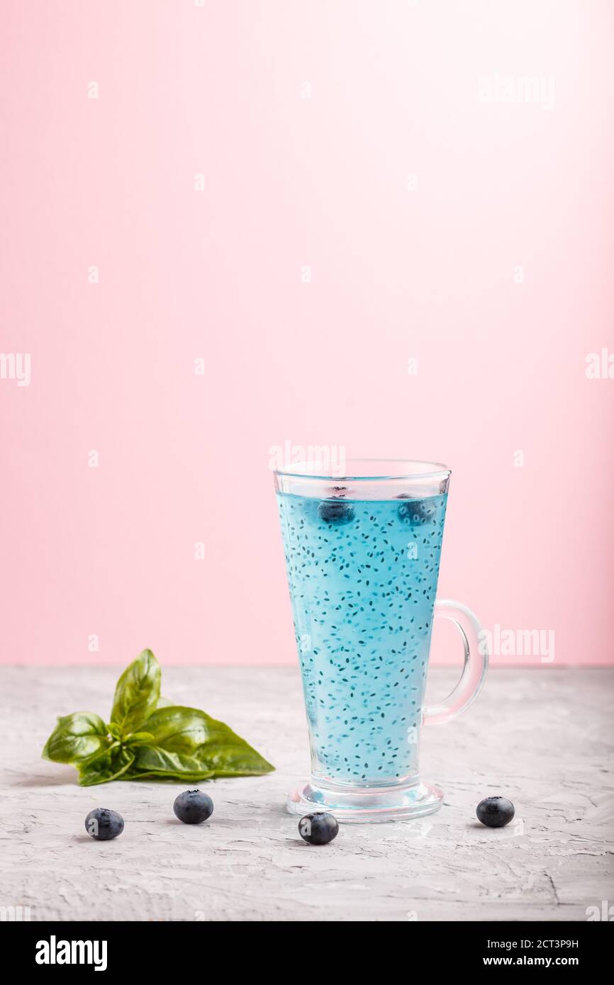 Glass of blueberry blue colored drink with basil seeds on a gray and ...