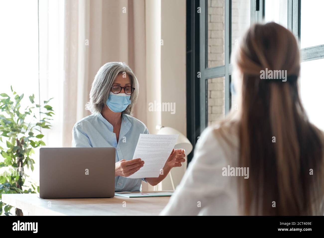 Old hr manager wearing face mask checking female applicant cv at job ...