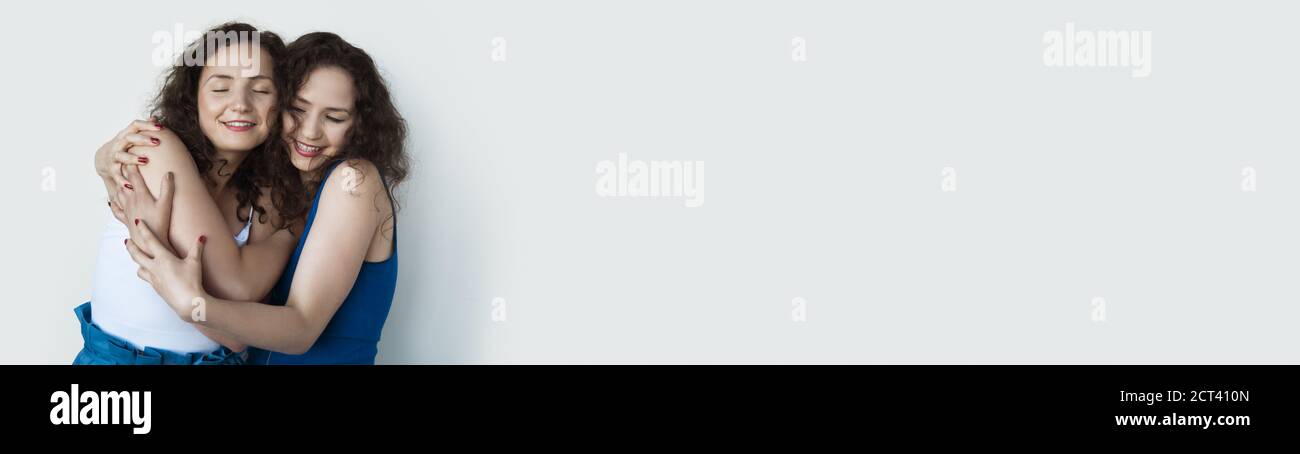 Caucasian twins embracing each other and smile posing on a gray studio ...