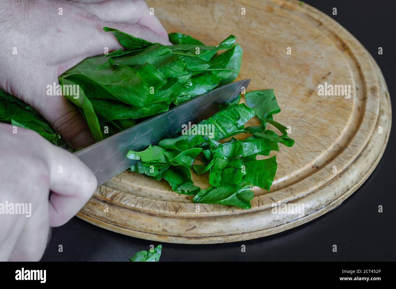 A male hand with a kitchen knife cuts the sorrel. Finely chopping green ...