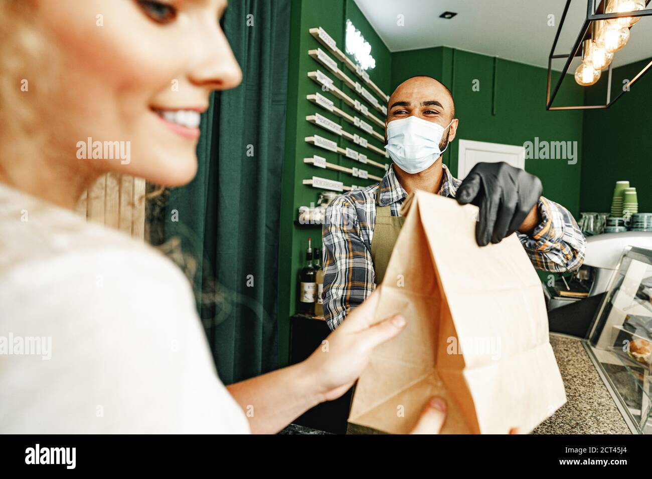 Male coffee shop worker giving ready order to the client wearing face ...