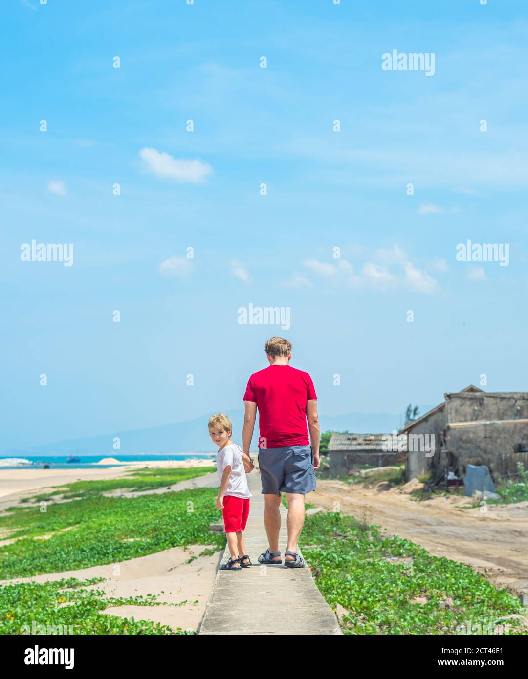 Father son walk along narrow concrete path, sea blue clear sky green ...