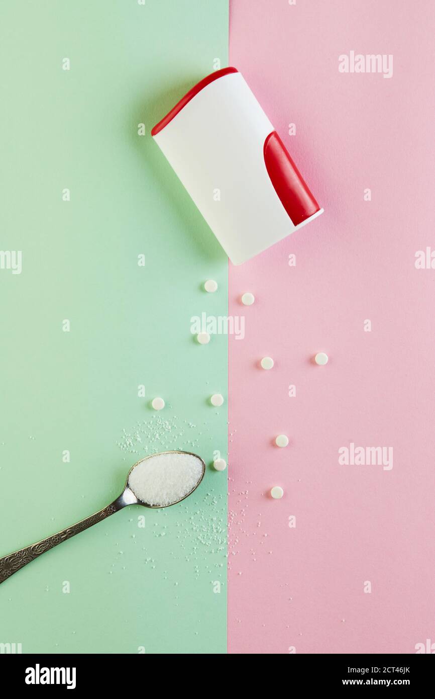 Sugar substitute tablets and natural sweetener powder on a green-pink ...