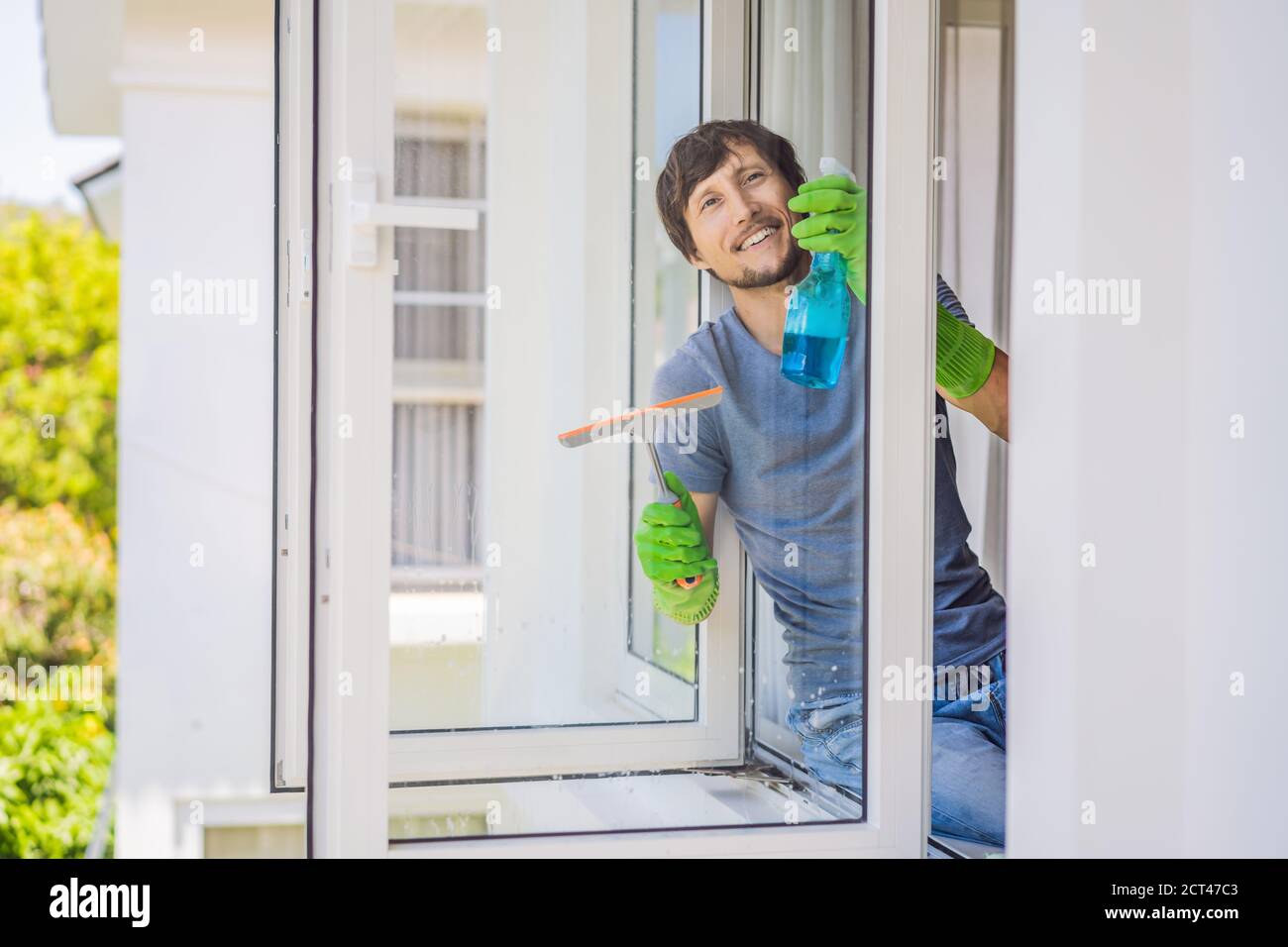 A young man cleaning the window with a window cleaner Stock Photo - Alamy