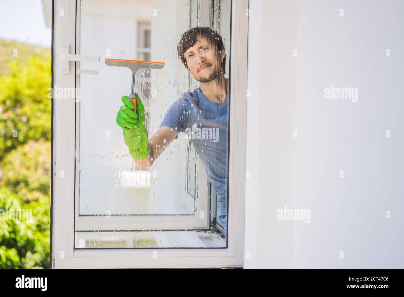 A young man cleaning the window with a window cleaner Stock Photo - Alamy