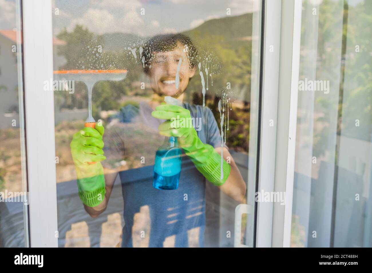 A young man cleaning the window with a window cleaner Stock Photo - Alamy