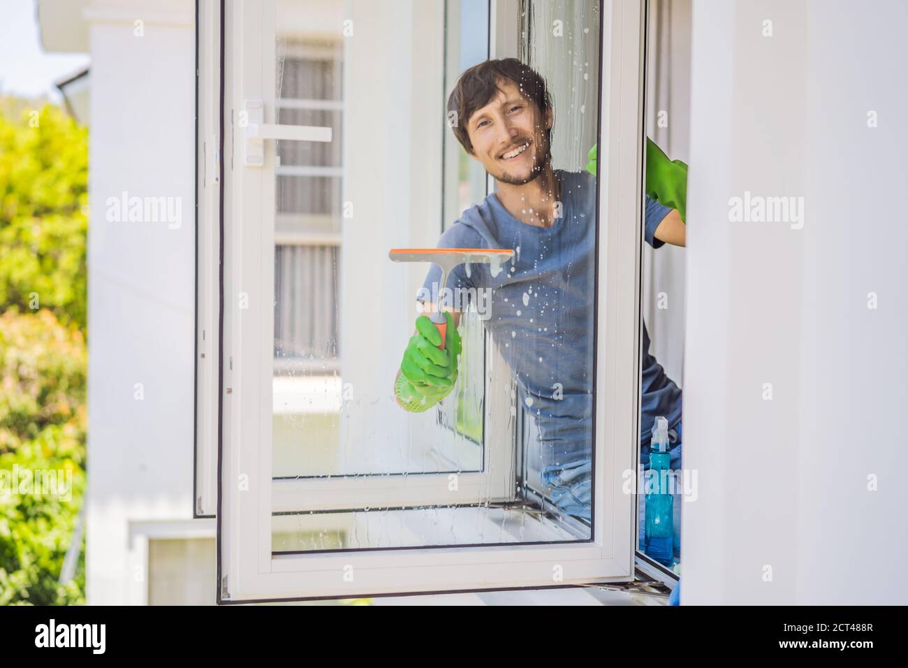 A young man cleaning the window with a window cleaner Stock Photo - Alamy