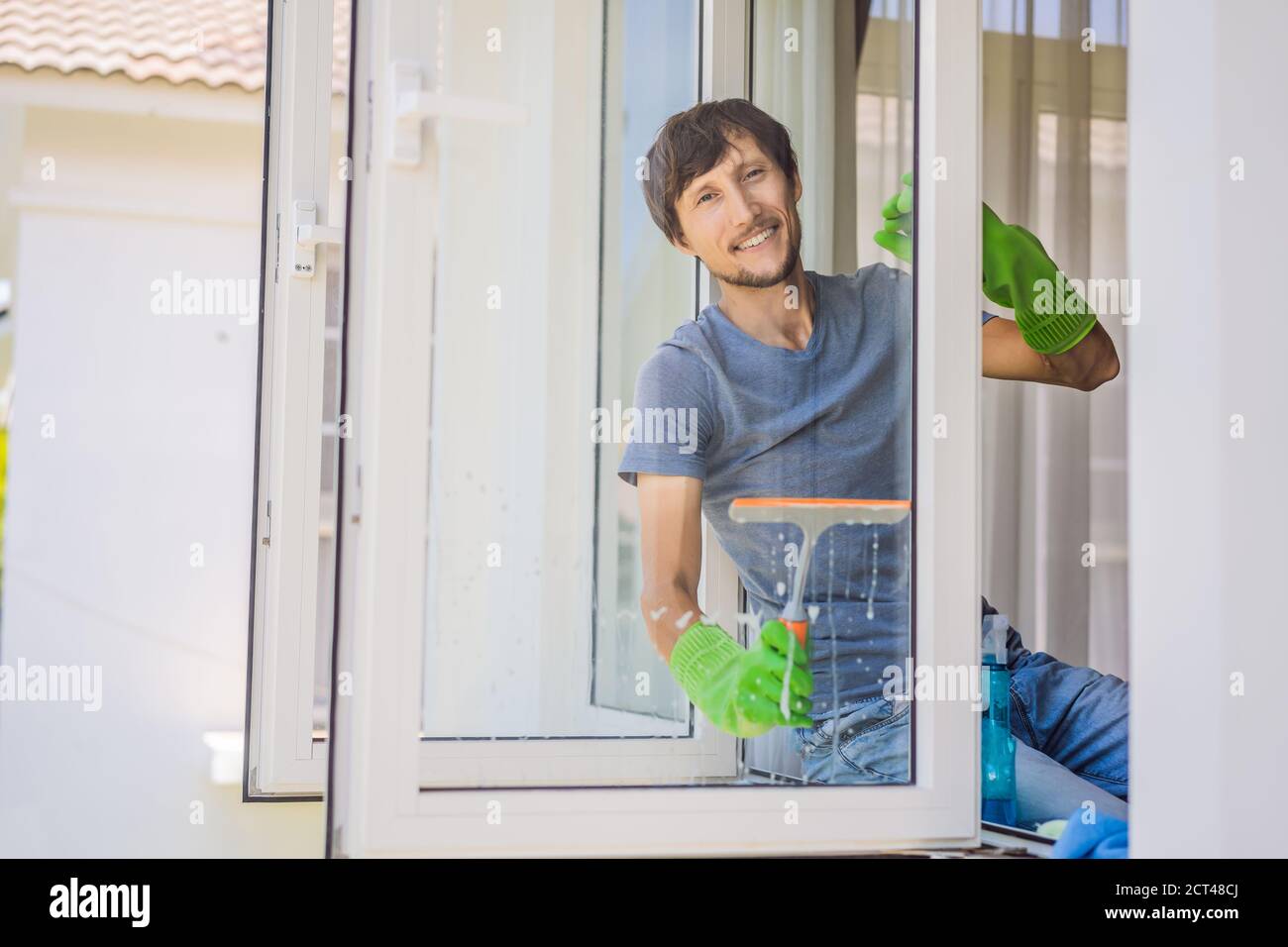 A young man cleaning the window with a window cleaner Stock Photo - Alamy