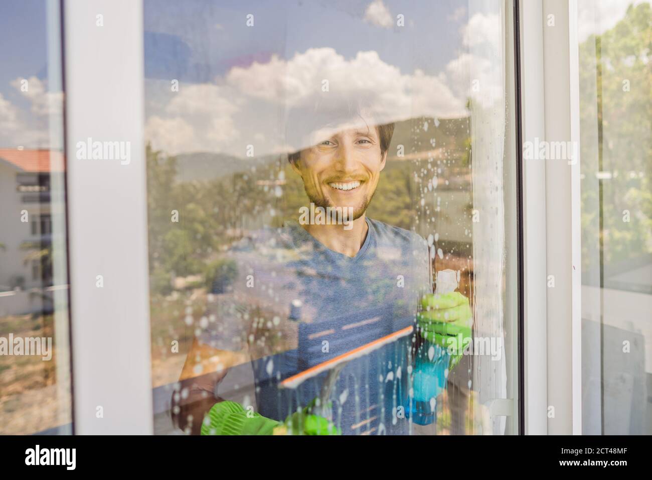 A young man cleaning the window with a window cleaner Stock Photo - Alamy