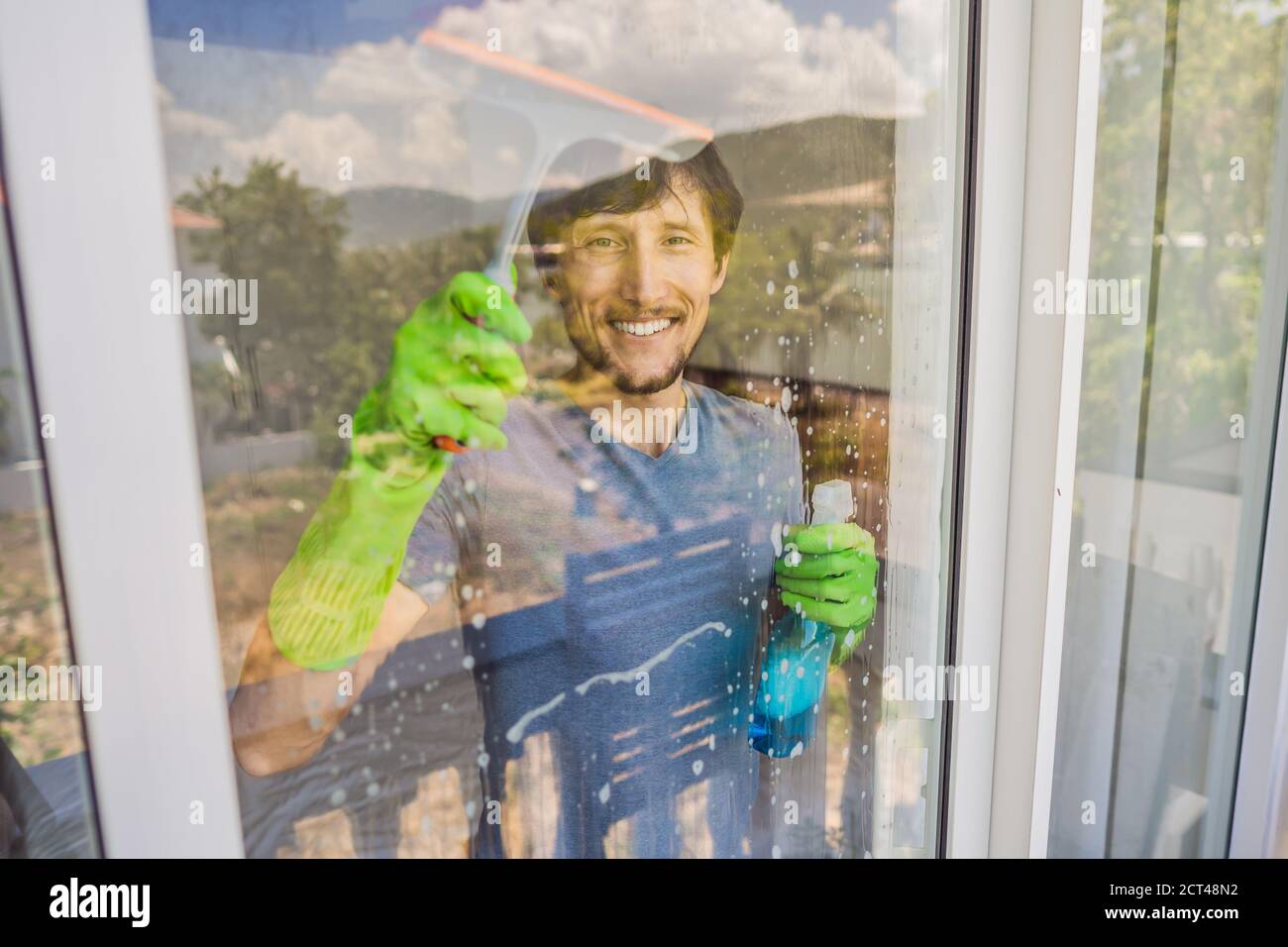 A young man cleaning the window with a window cleaner Stock Photo - Alamy