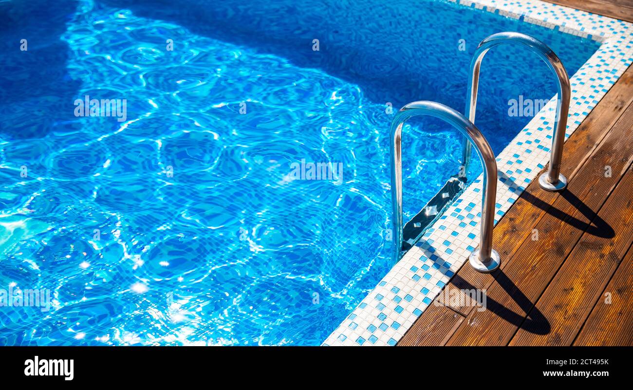 Blue swimming pool with grab ladder teak wood flooring stripes sunlight ...