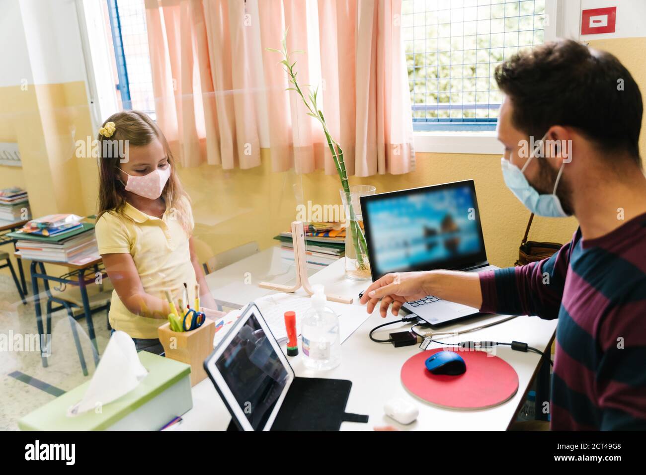Student with a mask handing over homework to the teacher through a ...